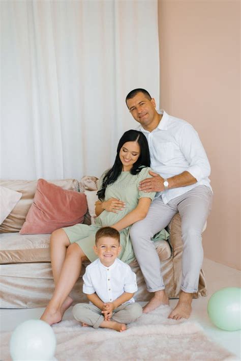 Pregnant Woman Is Sitting On A Sofa Surrounded By Her Husband And Son