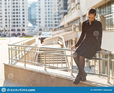 Teenager Brunette Girl With Long Hair Sits On The Railing In City Stock