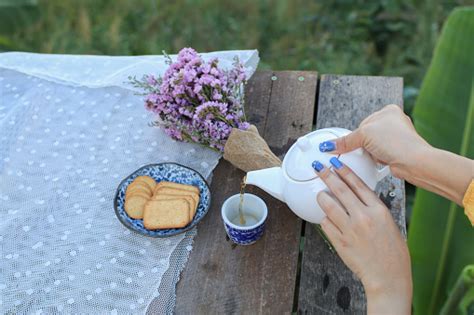 비스킷과 보라색 꽃과 함께 흰색 찻 주전자에서 차를 붓는 손 나무 테이블 풍경 배경에 산의 전망 갈색에 대한 스톡 사진 및 기타