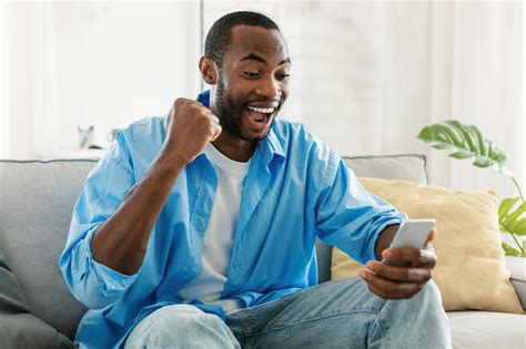 Premium Photo Great News Overjoyed Black Man Holding Smartphone And