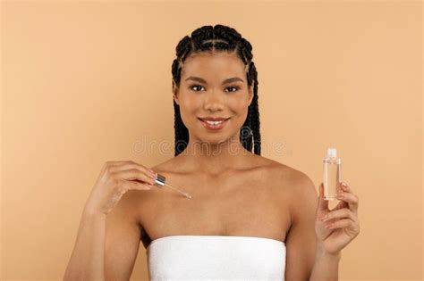 Young Black Woman With Braided Hair Applying Beauty Oil To Her Chest