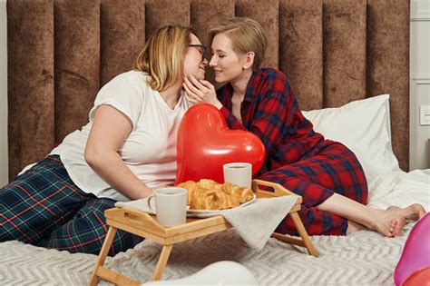 잠옷을 입은 레즈비언 부부는 접이식 테이블과 빨간 하트 모양의 풍선에 아침 식사 앞에 침대에 누워 2명에 대한 스톡 사진 및