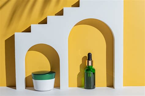 노란색 배경에 흰색 장식 아치에 피펫과 크림 항아리가 있는 녹색 유리 병 화장품 액체 제품 광고 및 판촉을위한 템플릿 0명에
