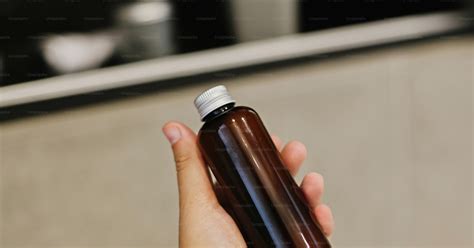 플라스틱이 없는 천연 유기농 필수품이 있는 세련된 검은색 선반을 배경으로 현대적인 욕실의 유리병에 천연 강장제 또는 샴푸를 들고 있습니다 폐기물 제로 개념 사진