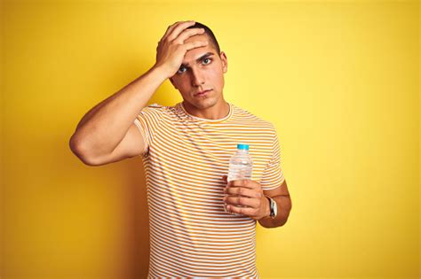 노란 고립 된 배경 위에 플라스틱 물병을 들고 젊은 잘 생긴 남자는 머리에 손으로 스트레스 수치와 깜짝 얼굴 분노와 좌절에 충격 실수에 대한 두려움과 화가 남자에 대한 스톡