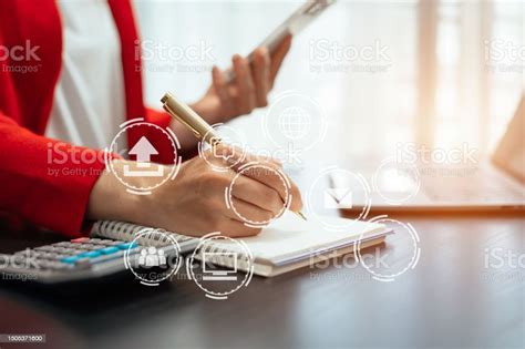 여성 사업가는 스마트폰을 사용하고 아침에 사무실 책상에 있는 노트북에 메모를 한다 Brand Name Smart Phone에