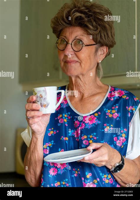 Granny With Old Smock Apron Glasses And Wig In The Kitchen Holding