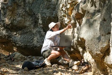 Female Geologist Using Laptop Computer Examining Nature Analyzing Rocks Or Pebbles Researchers
