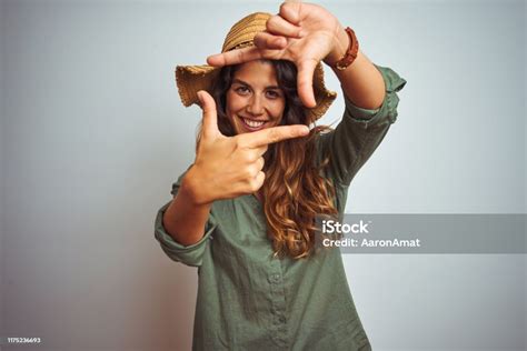 행복한 얼굴로 손과 손가락으로 프레임을 만드는 흰색 고립 된 배경 위에 녹색 셔츠와 모자를 입고 휴가에 젊은 아름다운 여성 창의력과 사진 개념 갈색 머리에 대한 스톡 사진
