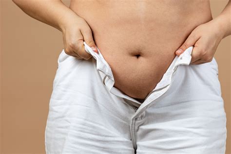 베이지 색 배경에 흰색 셔츠를 지퍼로 올리려고하는 두꺼운 통통한 복부를 가진 여성의 클로즈업 내장 지방 몸 양성 갑작스런 체중