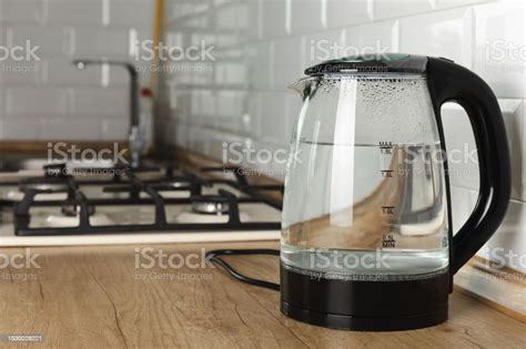 주방의 나무 테이블에 있는 현대적인 전기 투명 주전자 물을 끓이고 차를 만들기위한 주전자 뜨거운 음료를 만들기위한 가전 제품