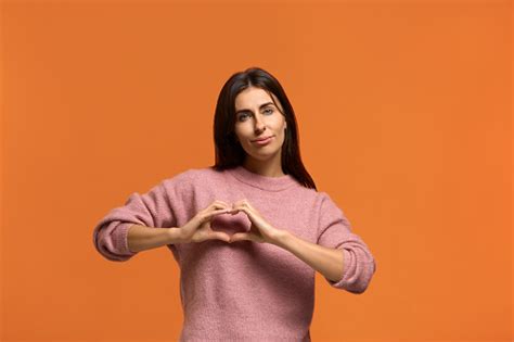 사랑 평화 단합을 상징하는 마음의 모양으로 손을 잡고 있는 잘 생긴 여성 스웨터를 입고 애정을 표현하는 하트 모양의 손 짓을
