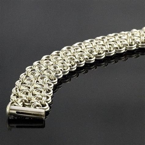 A Silver Chain Bracelet On A Black Surface With A Metal Clip In The