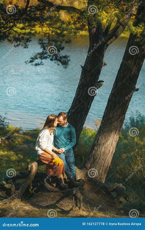 Beau Couple Romantique Assis Sous Larbre à La Rive De La Rivière Et Sembrassant Le Jour D