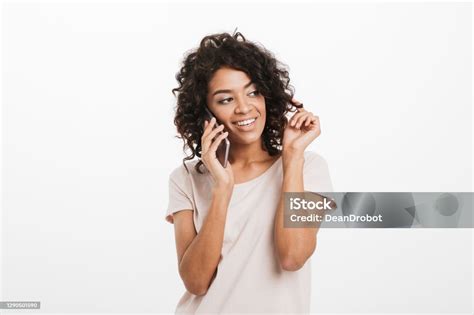 트렌디 한 헤어 스타일을 가진 귀여운 유쾌한 여성의 초상화는 기본 티셔츠를 입고 휴대 전화로 이야기하고 흰색 배경에 고립 된