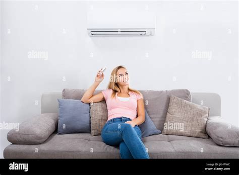 Young Happy Woman Sitting On Couch Operating Air Conditioner With