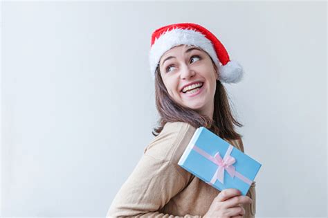 흰색 배경에 고립 된 손에 파란색 선물 상자를 들고 빨간색 산타 클로스 모자에 아름다운 소녀 젊은 여성 초상화 진정한 감정 해피