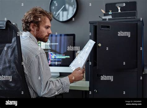 Side View Portrait Of Bearded It Programmer Reading Document At Workplace With Code Lines In