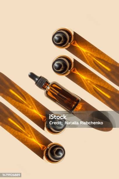 베이지색 배경에 햇빛에 스포이드 뚜껑이 있는 유리 바이알의 모형의 밝은 패턴 딱딱한 그림자가있는 화장품 세럼이있는 표시가없는 용기 클로즈업 세로 이미지 갈색에 대한 스톡