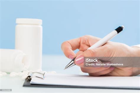 의사u2019s 는 흰색 의료 코트에 손을 처방전에 펜을 밀어 파란색 배경에 알약이있는 두 개의 흰색 항아리 의학의 개념 심장학