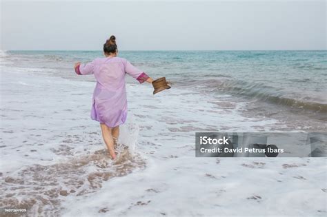 여름에 해변에서 물위에서 달리는 보라색 드레스와 모자를 쓰고 다리에 정맥류가있는 인식 할 수없는 곡선 시니어 여성복사 공간
