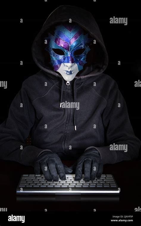 A Hooded Person With A Mask Typing On A Computer Keyboard Low Key