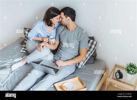 Lovely Romantic Couple Going To Kiss Look At Each Other As Sit On Bed