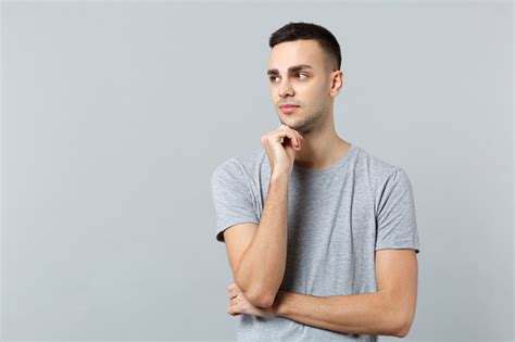 캐주얼 한 옷에 잠겨있는 젊은 남자의 초상화 옆을 찾고 스튜디오에서 회색 벽 배경에 고립 된 턱에 손을 소품을 넣어 사람들은