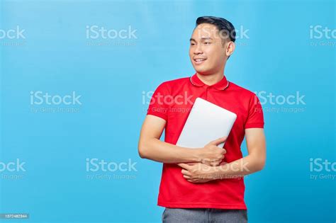 빨간 셔츠를 입고 노트북을 들고 파란색 배경에 고립 된 복사 공간을 바라 보는 아시아 잘 생긴 청년의 초상화 25 29세에 대한 스톡 사진 및 기타 이미지 Istock