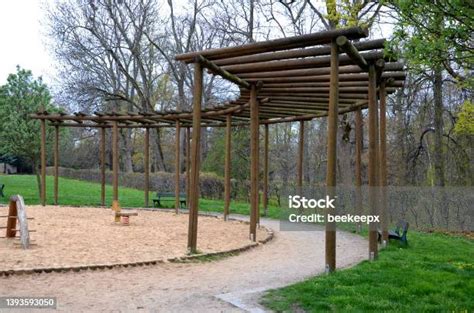 둥근 Pergola 아이들을위한 놀이 요소가있는 모래 구덩이 주위에 나무 기둥으로 만든 트렐리제 주변에는 길과 잔디밭이 있습니다