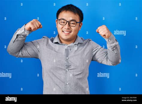 Young Chinese Man Standing Over Blue Background Showing Arms Muscles