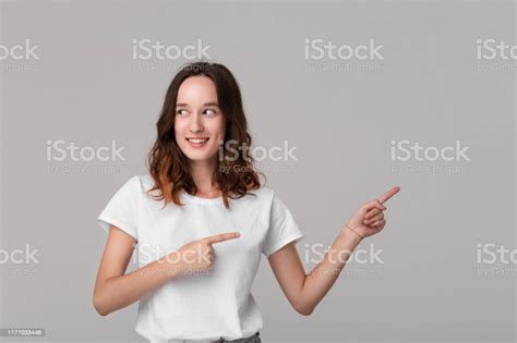 회색 배경 위에 고립 된 프레임의 오른쪽에있는 빈 공간을 가리키는 흰색 티에 예쁜 갈색 머리 여자 광고 의 공간을 복사합니다 T