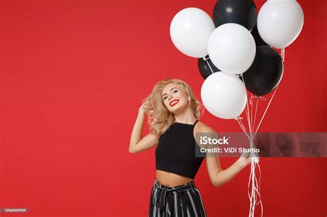 스튜디오에서 밝은 빨간 벽 배경에 고립 포즈 검은 옷을 입고 예쁜 젊은 여자 소녀 여성의 날 생일 휴일 파티 개념 복사 공간을 모의합니다 축하 공기 풍선을 들고 가방에 대한