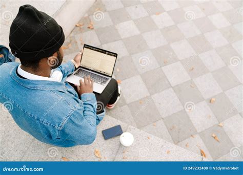 Black Man With Headphones Working With Laptop While Sitting On Bench