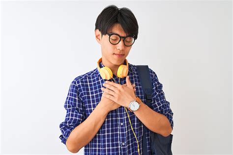 배낭과 헤드폰을 착용한 중국인 학생은 고립된 흰색 배경 위에 손을 얹고 눈을 감고 얼굴에 감사하는 제스처를 취하며 미소를 짓고