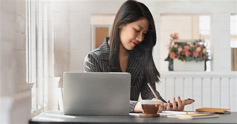 편안한 사무실을 배경으로 현대적인 작업 테이블에서 컴퓨터 노트북 앞에 앉아 메모를 하고 스마트폰을 손에 들고 보는 젊은 사업가의