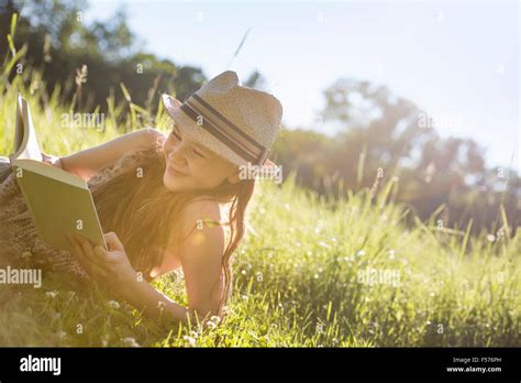 A Young Girl In A Straw Hat Lying On The Grass Reading A Book Stock