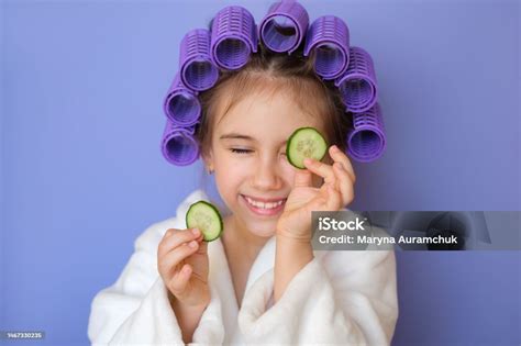 고데기로 감싼 머리를 가진 작은 아가씨가 신선한 오이 조각을 눈에 씌운다 뷰티 스파에 대한 스톡 사진 및 기타 이미지 뷰티
