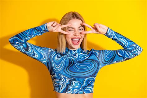 밝은 노란색 배경에 장난기 많은 손가락 제스처로 포즈를 취하며 행복과 자신감을 표현하는 세련된 파란색 상의를 입은 즐거운 젊은 여성 20 24세에 대한 스톡 사진 및 기타