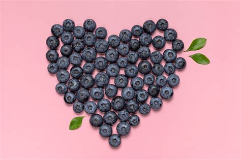 분홍색 배경에 하트 모양의 녹색 잎이있는 신선한 육즙 블루 베리 블루베리 배경 플랫 레이 상단 보기 창조적 인 사랑 개념 건강한