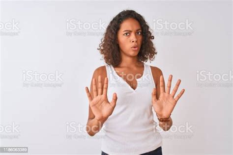 고립 된 흰색 배경 위에 서있는 캐주얼 한 티셔츠를 입은 젊은 브라질 여성은 두려움과 역겨운 표정으로 거절과 거부를 보여주는