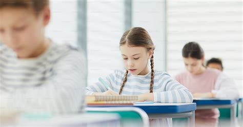 갈색 머리를 가진 젊은 백인 소녀가 줄무늬 시트셔츠를 입고 현대 클라룸의 학교 책상에 앉아 노트북에 무언가를 쓰고 있습니다 사진 Unsplash의 퀴즈 이미지