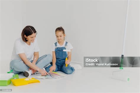 작은 소녀와 그녀의 어머니는 바닥에 앉아 색상 팔레트에 주의 깊게 보고 그림 방에 가장 적합한 색상을 선택 건물 도구를 사용하여