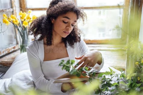Pretty African American Girl Reading Book Sitting On Windowsill Stock
