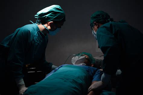 환자는 수술실의 수술실에 누워 있는 의료 용 인공호흡기를 착용하고 외과 의사는 병원에서 증상을 주시하기 위해 옆에 서 있다 3