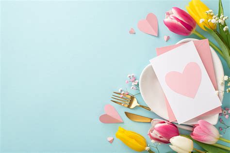 세련된 어머니의 날 테이블 세팅 컨셉 파스텔 블루 배경에 접시 수저 튤립 인사말 카드 장식용 하트가 평평하게 놓여 있다 텍스트