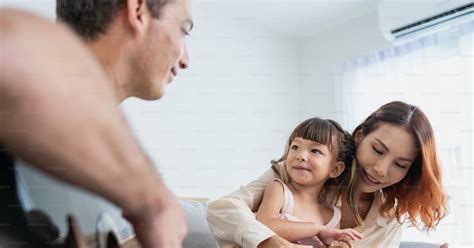 집에서 어린 아이와 함께 기타를 연주하는 아시아 젊은 부부 매력적인 아름다운 부모님은 소파에 앉아 집안의 거실에서 노래를 부르는 어린 딸과 여가 시간을 보냅니다 사진