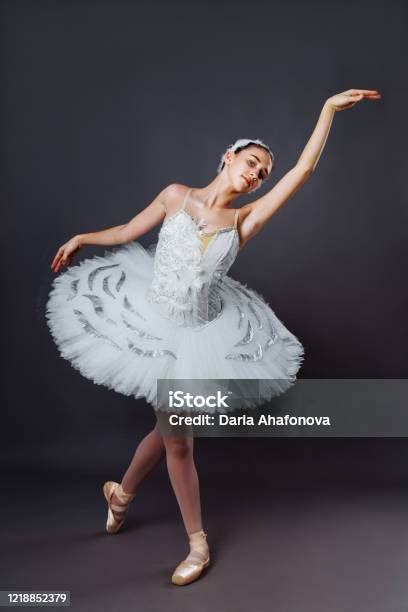 백조 호수에서 백조의 투투 스커트에 젊은 아름다운 우아한 백인 발레리나 연습 발레 위치의 초상화 발가락에 서있는 회색 배경에 스튜디오에서 클래식 발레 댄서