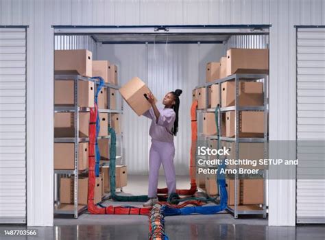 흰 벽으로 둘러싸인 차고에 선반과 골판지 수납함이 있는 여자가 상자를 들고 서 있다 이더넷 케이블 묶음은 선반 유닛 사이의 차고로 연결됩니다 클라우드 컴퓨팅 또는 클라우드