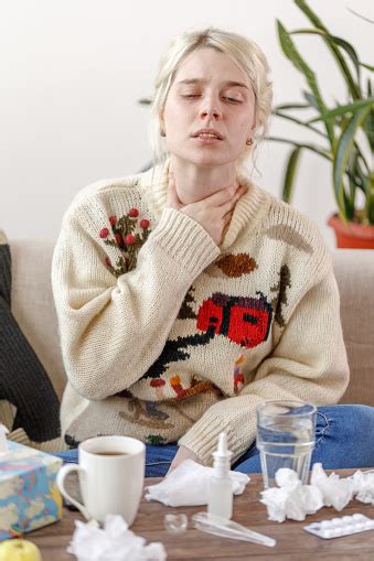 스웨터를 입은 소녀는 소파에 앉아 아프다 감기와 독감 환자는 감기에 걸렸고 아프고 목이 아팠습니다 인후통을 가진 건강에 해로운 소녀 감기와 독감에 대한 스톡 사진 및 기타